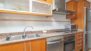 Uma cozinha com armários de madeira, pia de aço inoxidável, micro-ondas, lava-louças e geladeira.