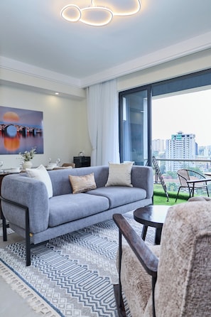 Uma sala de estar moderna com um sofá cinzento, um tapete estampado, uma mesa de jantar e vista para a cidade através de grandes janelas.