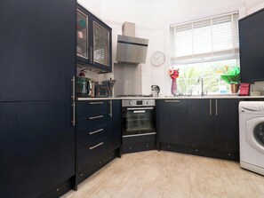 Cozinha compacta com armários escuros, forno embutido, micro-ondas e máquina de lavar.