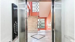 Um elevador com painel de controle, chão de azulejos e escadas que levam a um quarto com janela e porta.