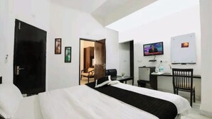 Quarto de hotel com cama, escrivaninha, cadeira, televisão e obras de arte nas paredes.