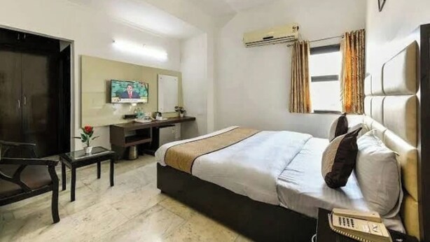 Quarto de hotel com cama, escrivaninha, televisão e ar condicionado.