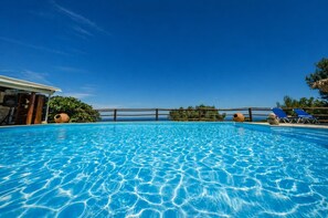 Piscina azul límpida com espreguiçadeiras e cerca de madeira.