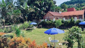Um jardim com mesas ao ar livre, um edifício com telhado vermelho e vegetação exuberante.