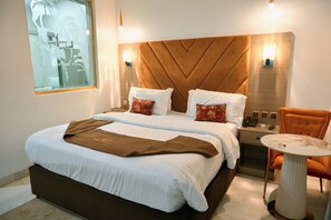 Quarto de hotel com uma cama grande, uma mesinha de cabeceira, uma cadeira e luminária na parede.
