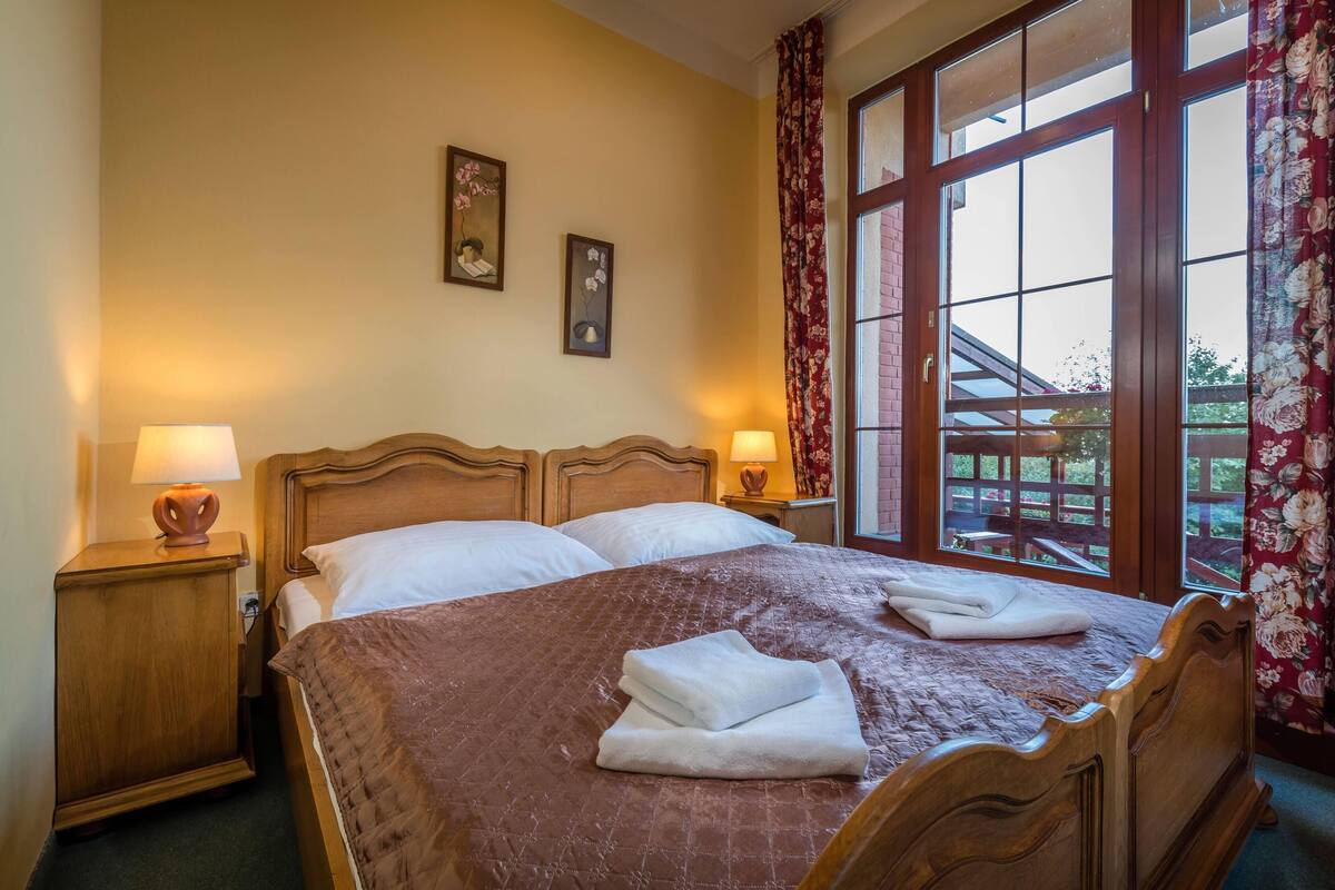 Quarto com cama de madeira, duas mesas de cabeceira com luminárias, janela com vista e duas imagens penduradas na parede.