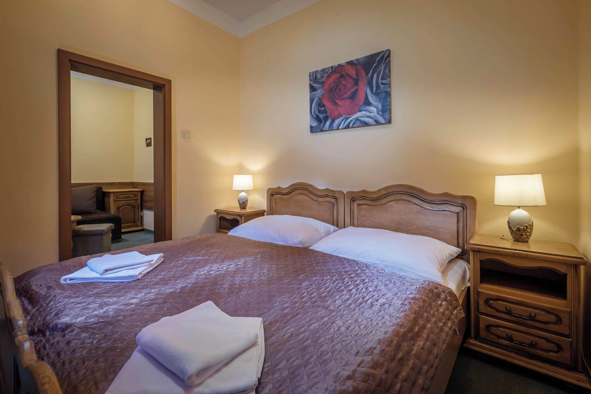 Quarto de hotel com uma cama grande, duas mesas de cabeceira com abajures, cabeceira de madeira, pintura de uma rosa e um espelho na parede esquerda.