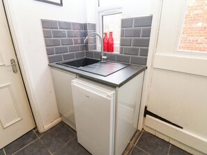 Uma cozinha compacta com pia embutida, um refrigerador pequeno e uma janela com vista para uma parede de tijolos.
