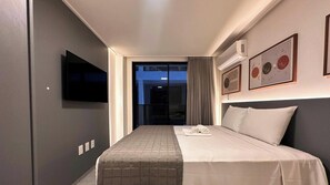 Quarto de hotel com cama, televisão de tela plana, janela com cortinas e obras de arte na parede.