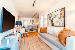 Uma sala de estar moderna com um sofá, televisão de tela plana, área de refeições e cozinha ao fundo.