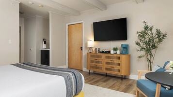 Quarto de hotel com cama, televisão, armário de madeira, máquina de café, planta e uma cadeira.