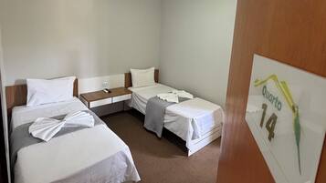 Quarto de hotel com duas camas de solteiro, uma mesa de cabeceira de madeira, luminária fixada na parede e uma porta com o símbolo de número.
