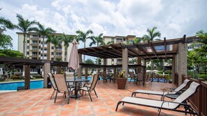 Uma área à beira da piscina com espreguiçadeiras, uma mesa e guarda-sóis.