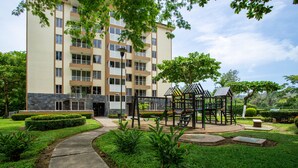 Um edifício com vários andares e um pátio central, rodeado por vegetação bem cuidada e um parquinho.