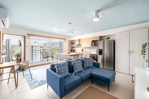Uma sala de estar moderna com sofá, um espaço de refeições com cadeiras, uma cozinha equipada e uma varanda com vista.