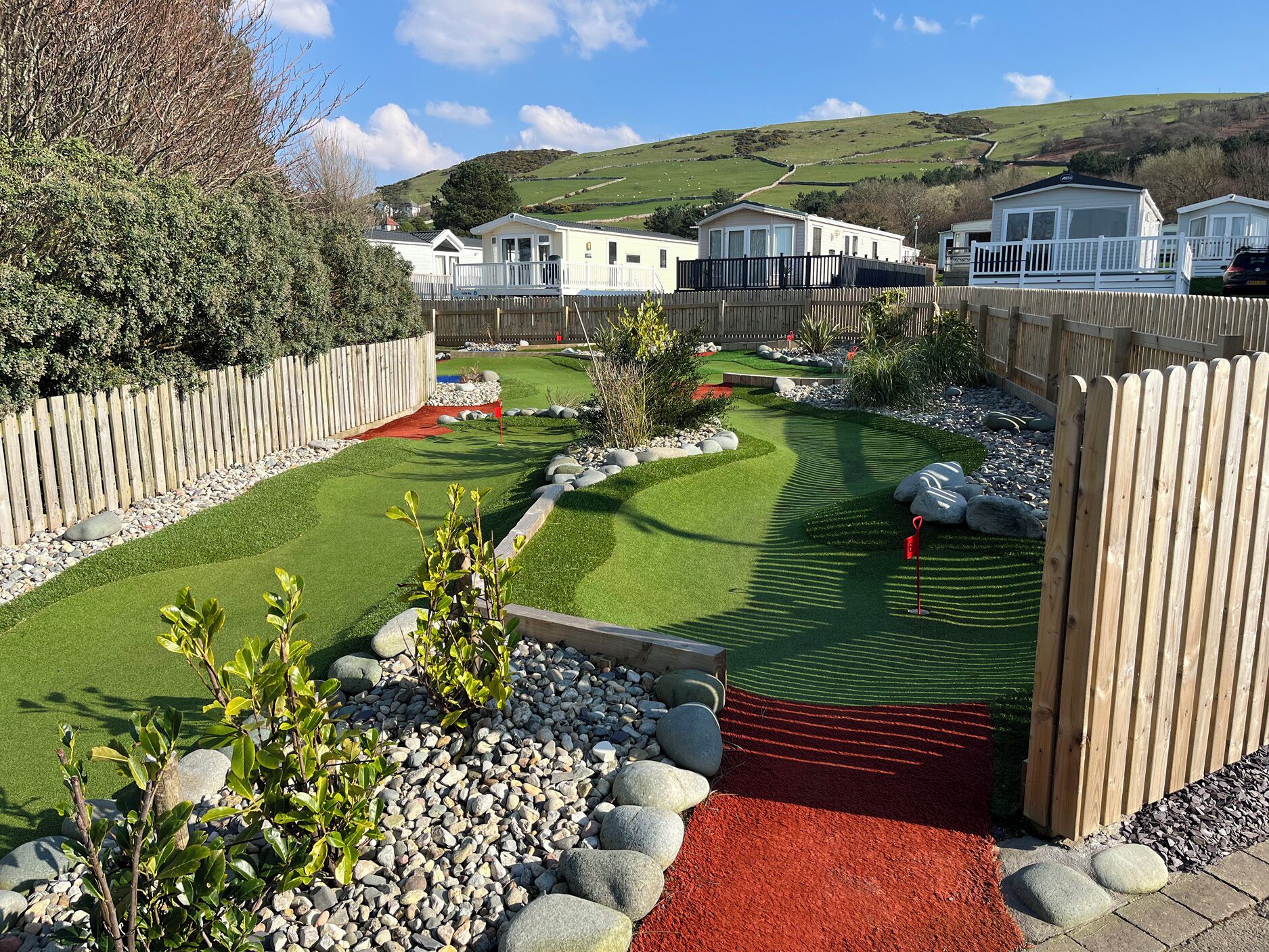 Uma área residencial com gramado bem cuidado, um caminho de tapete vermelho e cerca de madeira.
