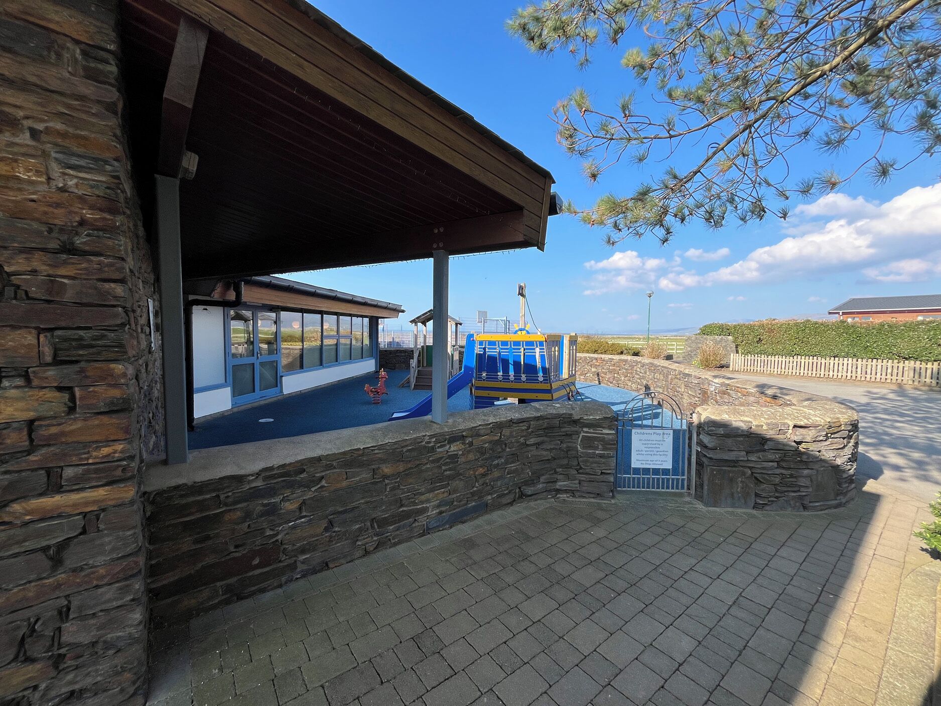 Um edifício de pedra com área externa coberta, espaço de recreação infantil e vista para a paisagem ao redor.