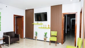 Uma sala de estar moderna com televisão de tela plana, duas poltronas, uma mesinha e prateleiras decorativas.