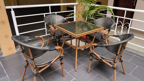 Conjunto de quatro cadeiras de vime com mesa de vidro em um pátio ladrilhado.