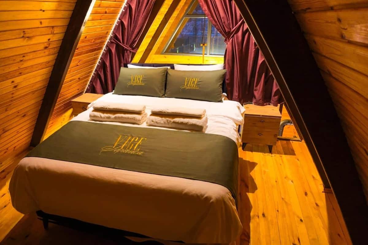 Um quarto acolhedor, com painéis de madeira, uma cama, um criado-mudo e uma janela com cortinas.
