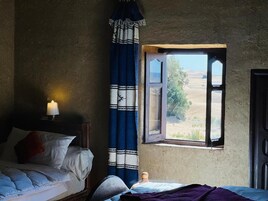 Um quarto com cama, janela com vista, luminária e cortina.