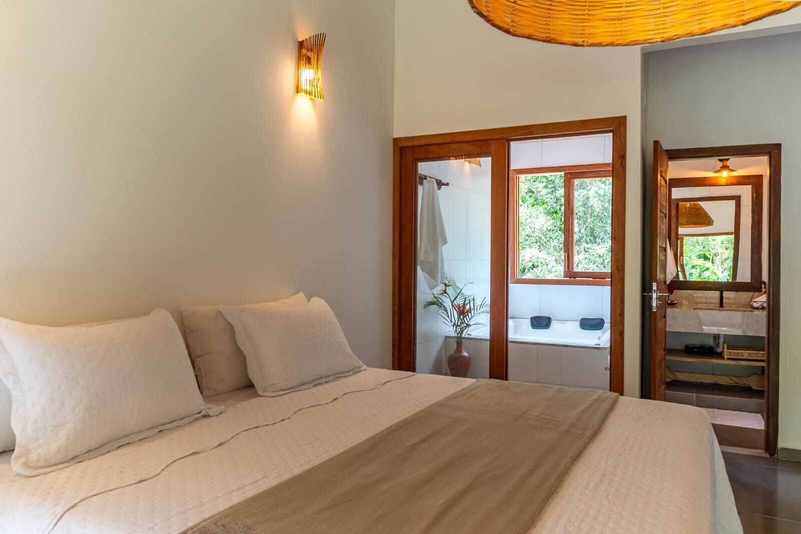 Um quarto com cama, luminária na parede, janela com vista e porta de madeira.