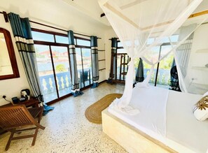 Quarto com cama, cadeira, janela com cortinas e vista para o exterior.