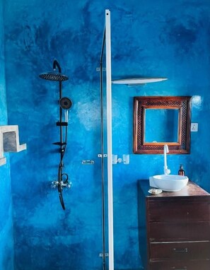 Casa de banho com parede azul, pia branca, armário de madeira e chuveiro com mangueira preta.
