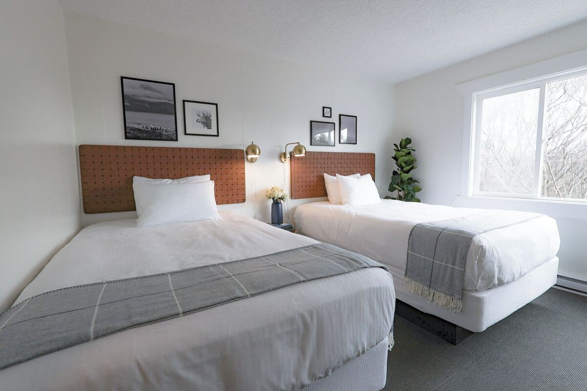 Quarto de hotel com duas camas, uma janela grande e quadros nas paredes.
