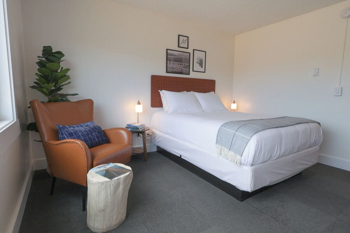 Quarto com cama, cadeira, mesinha e planta.