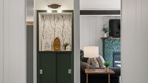Quarto com porta verde, luminária na parede, televisão em um suporte, um sofá e uma mesinha com abajur.