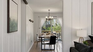 Uma área de refeições com mesa e cadeiras, um lustre e vista pela janela.