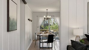 Uma área de refeições com mesa e cadeiras, um lustre e vista pela janela.