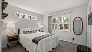 Quarto com uma cama, duas mesas de cabeceira, uma janela, um espelho e uma porta.