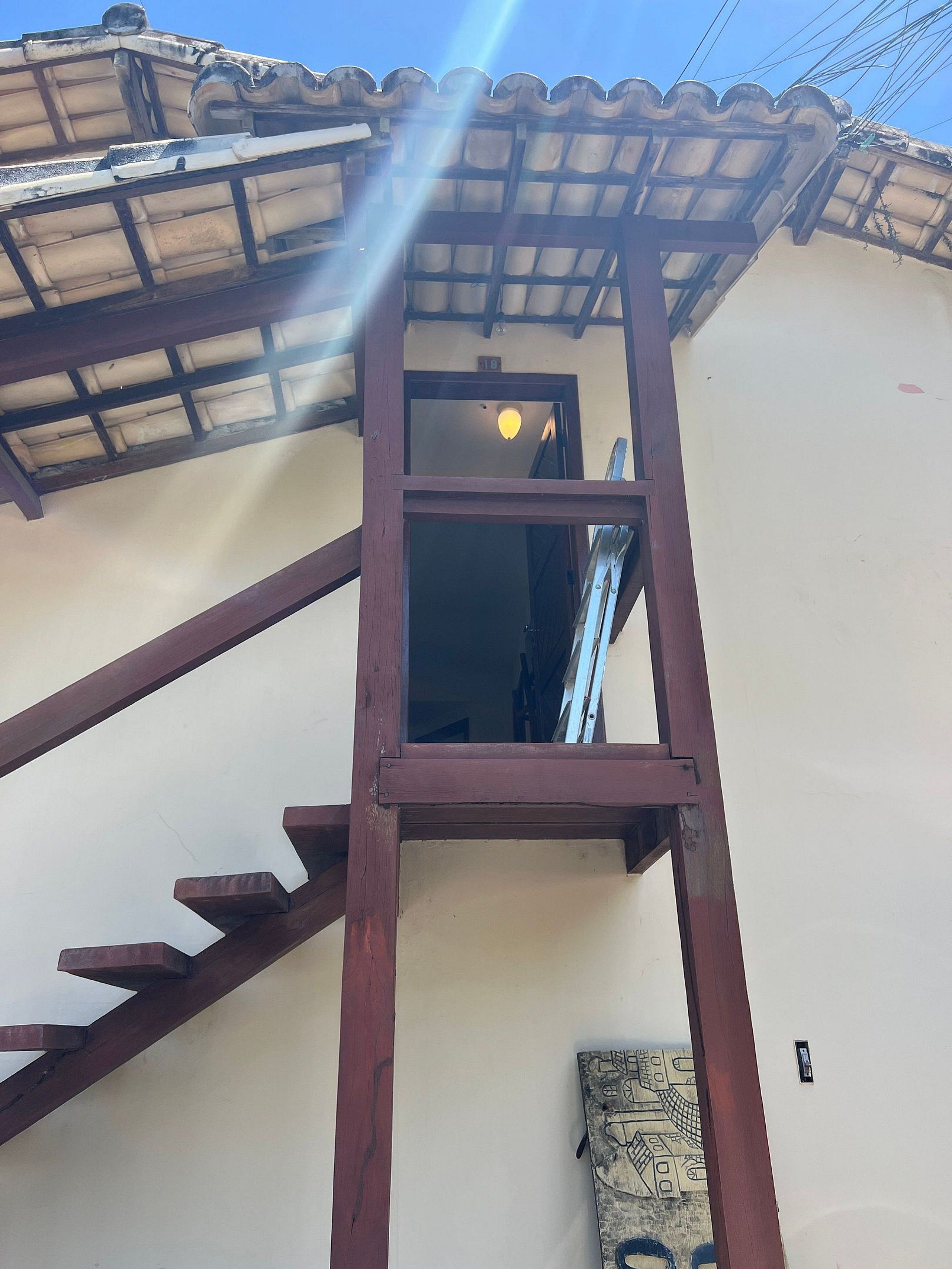 Escada de madeira que dá acesso a um quarto com telhado em cerâmica e uma janela.