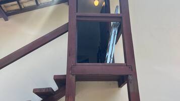 Escada de madeira que dá acesso a um quarto com telhado em cerâmica e uma janela.