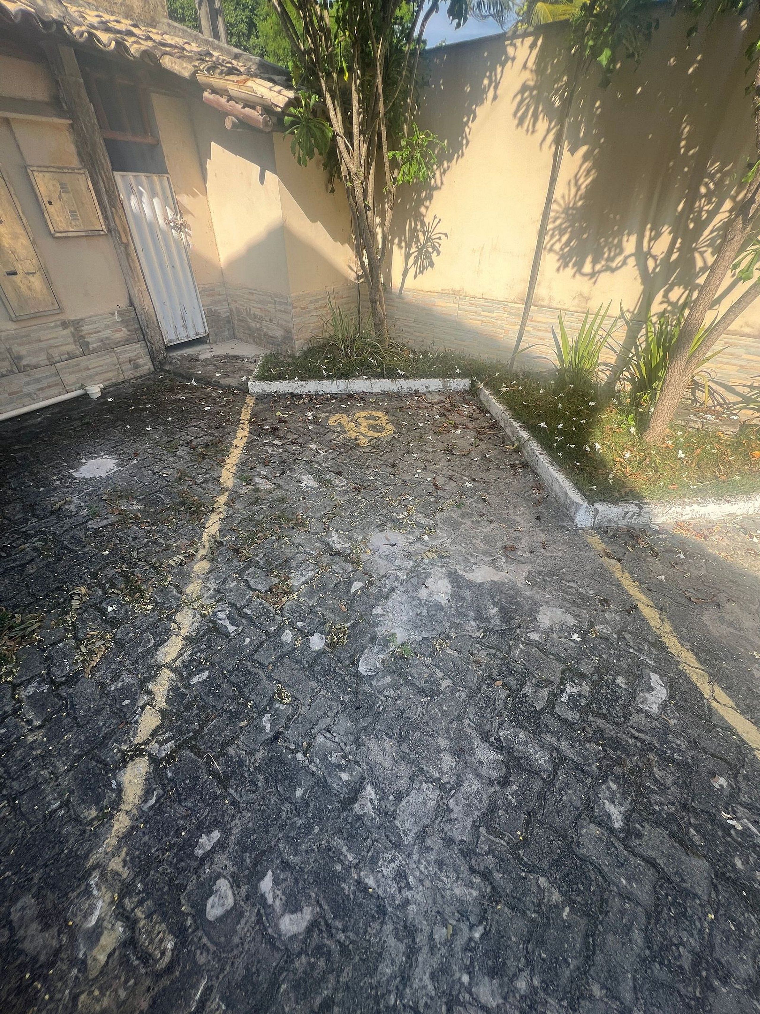 Pátio pavimentado com uma árvore, uma parede e uma porta de metal.