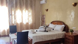 Um quarto com cama, mesa de cabeceira, cadeira, mesa, tapete e luminária de teto.