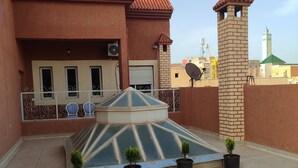 Terraço no telhado com uma área coberta pequena, plantas em vasos e uma torre de tijolos.