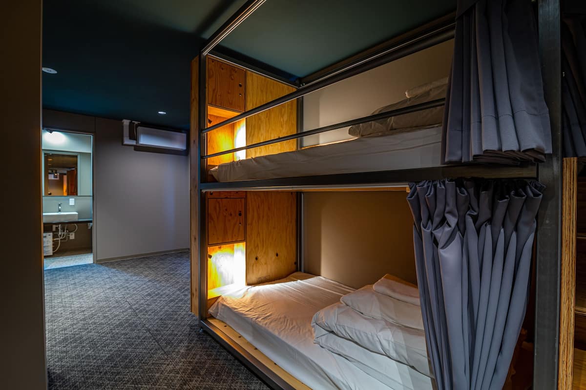 Quarto com beliche, cabeceira de madeira, espelho e banheiro ao fundo.
