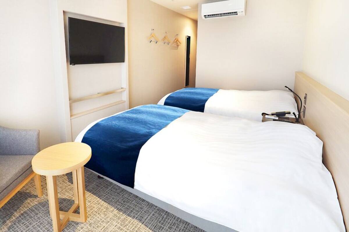 Quarto de hotel com duas camas, televisão, mesa pequena e sofá.