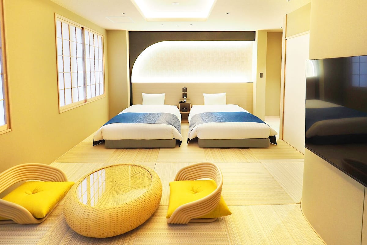 Quarto de hotel com duas camas, televisão, sofá e um futon.