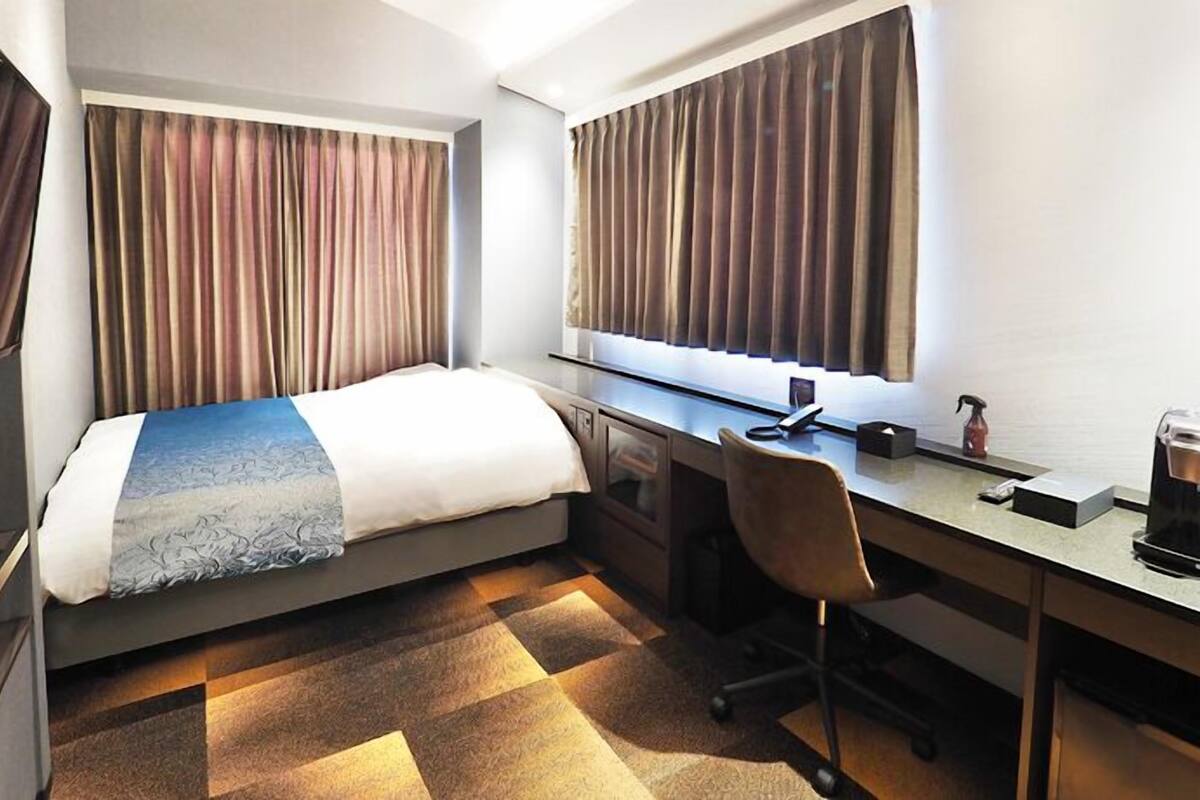 Quarto de hotel com cama, escrivaninha, cadeira e cortinas.
