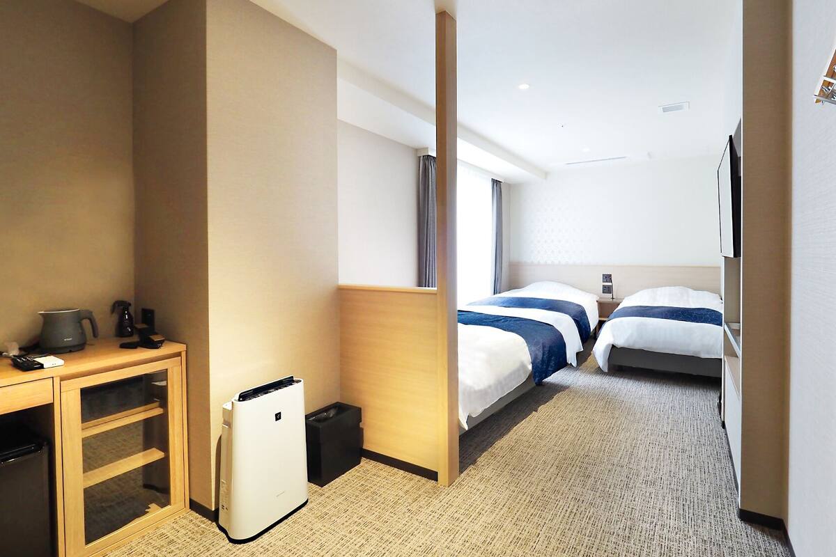 Quarto de hotel com escrivaninha, mini-frigorífico, cama com cabeceira e janela com cortinas.