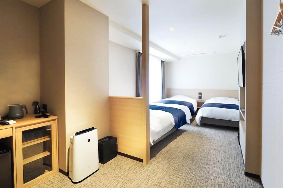 Quarto de hotel com escrivaninha, duas camas, um pequeno frigorífico e um cesto de lixo.
