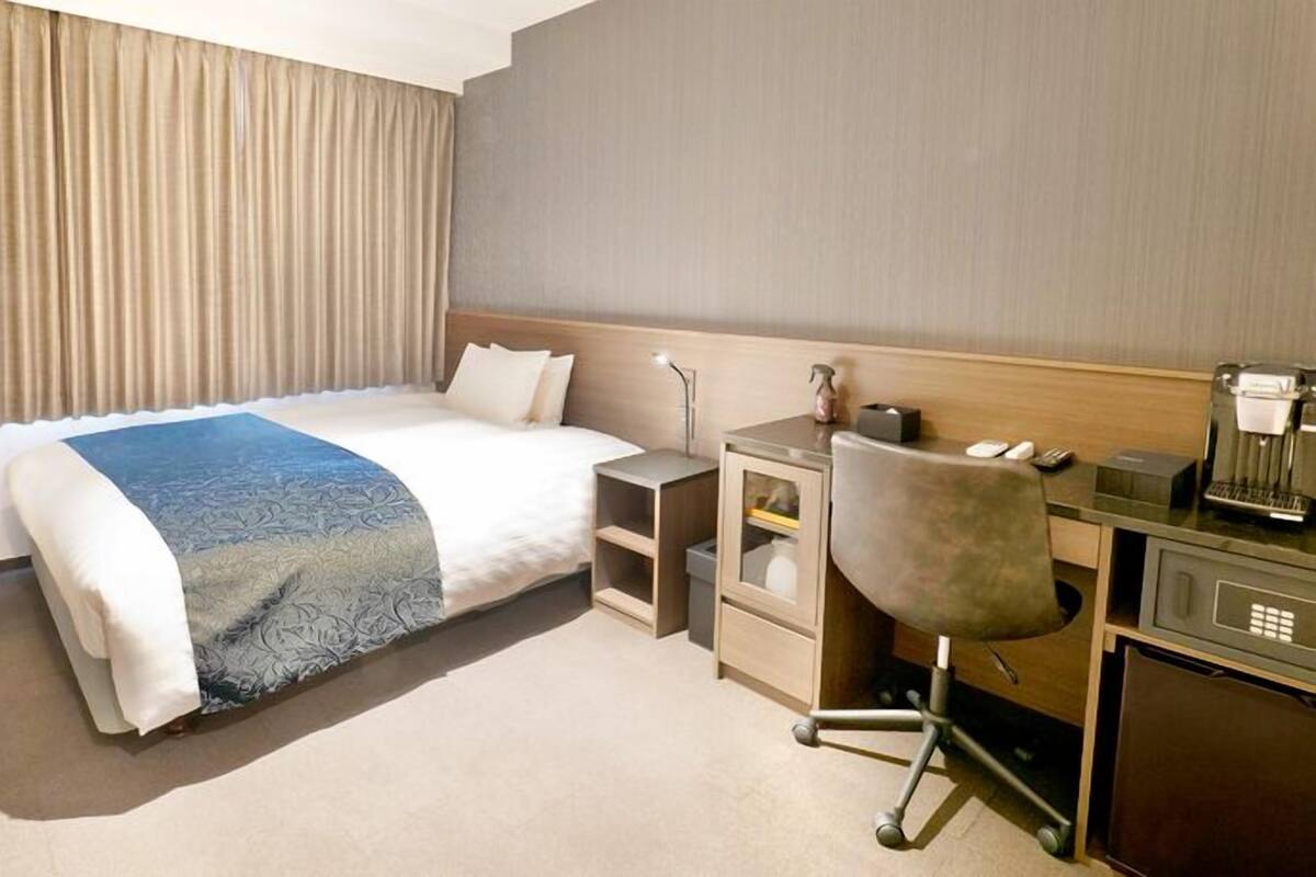 Quarto de hotel com cama, escrivaninha, cadeira e máquina de café.