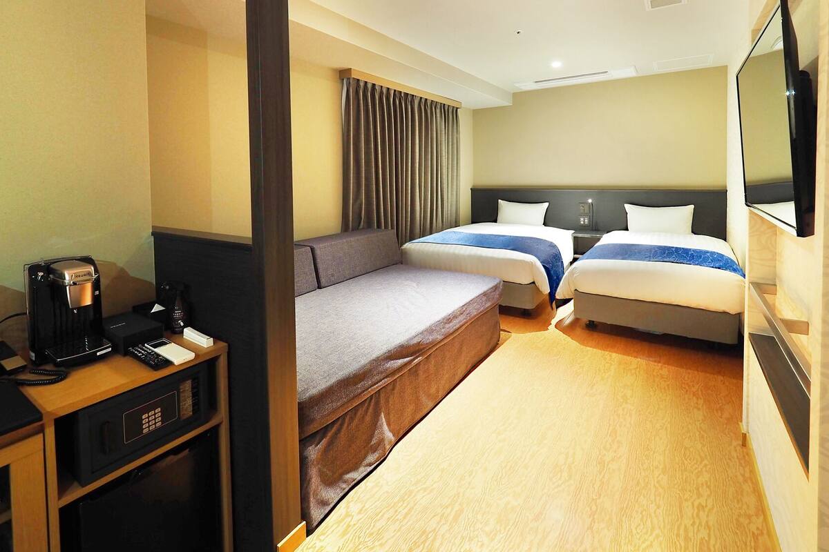 Quarto de hotel com duas camas, uma escrivaninha com cafeteira, computador e televisão.