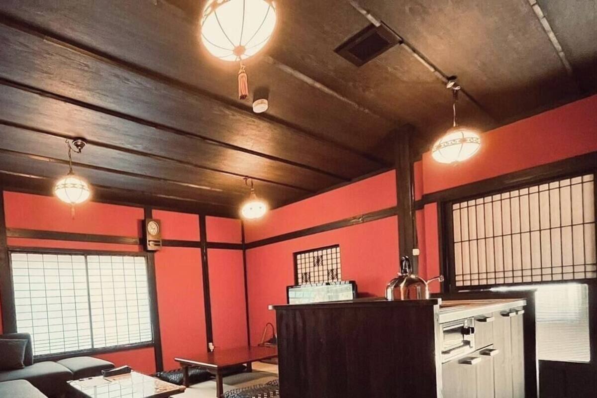 Um quarto com teto de madeira, uma porta tradicional japonesa deslizante, uma mesa pequena e um balcão com uma chaleira.