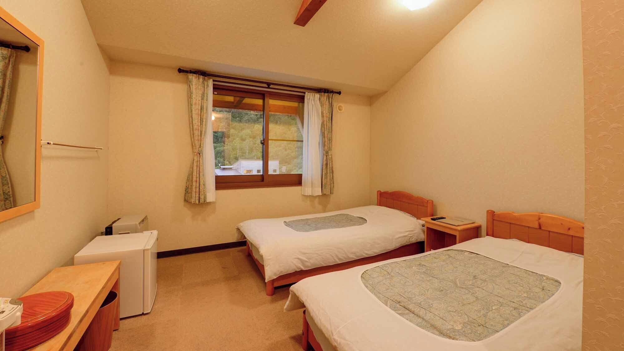 Quarto com duas camas, uma pequena mesa de cabeceira, um criado-mudo, uma janela com cortinas e um espelho na parede.
