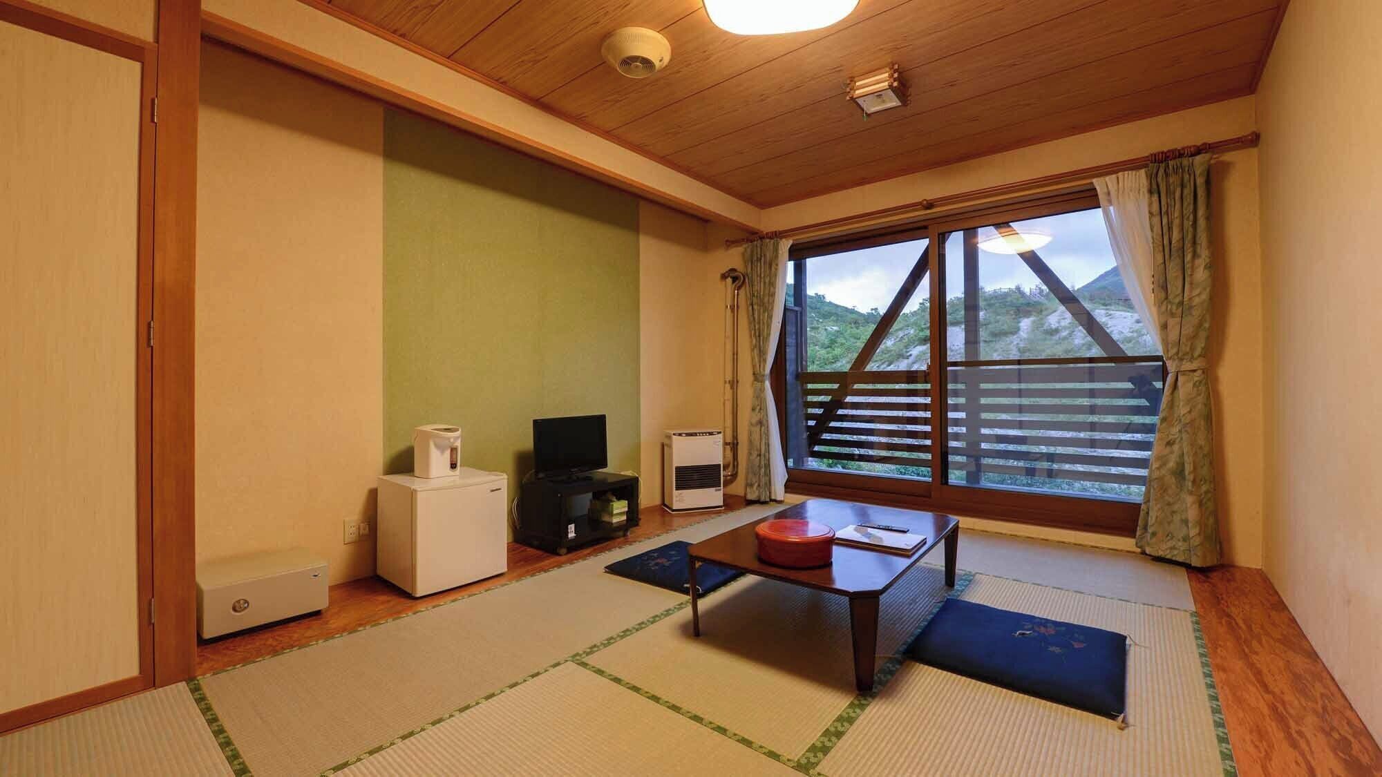 Quarto com piso de tatame, televisão, aquecedor e janela com vista para uma estrutura de madeira.